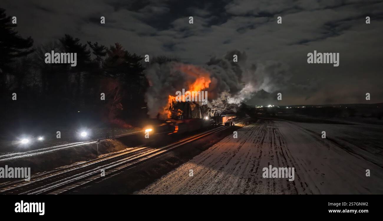 A train car is on fire next to snowy fields under a moonlit sky. Smoke ...