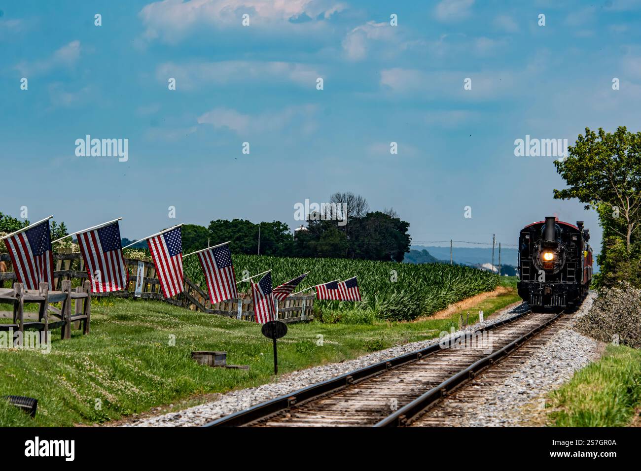 A classic steam train moves along the tracks in lush green countryside ...