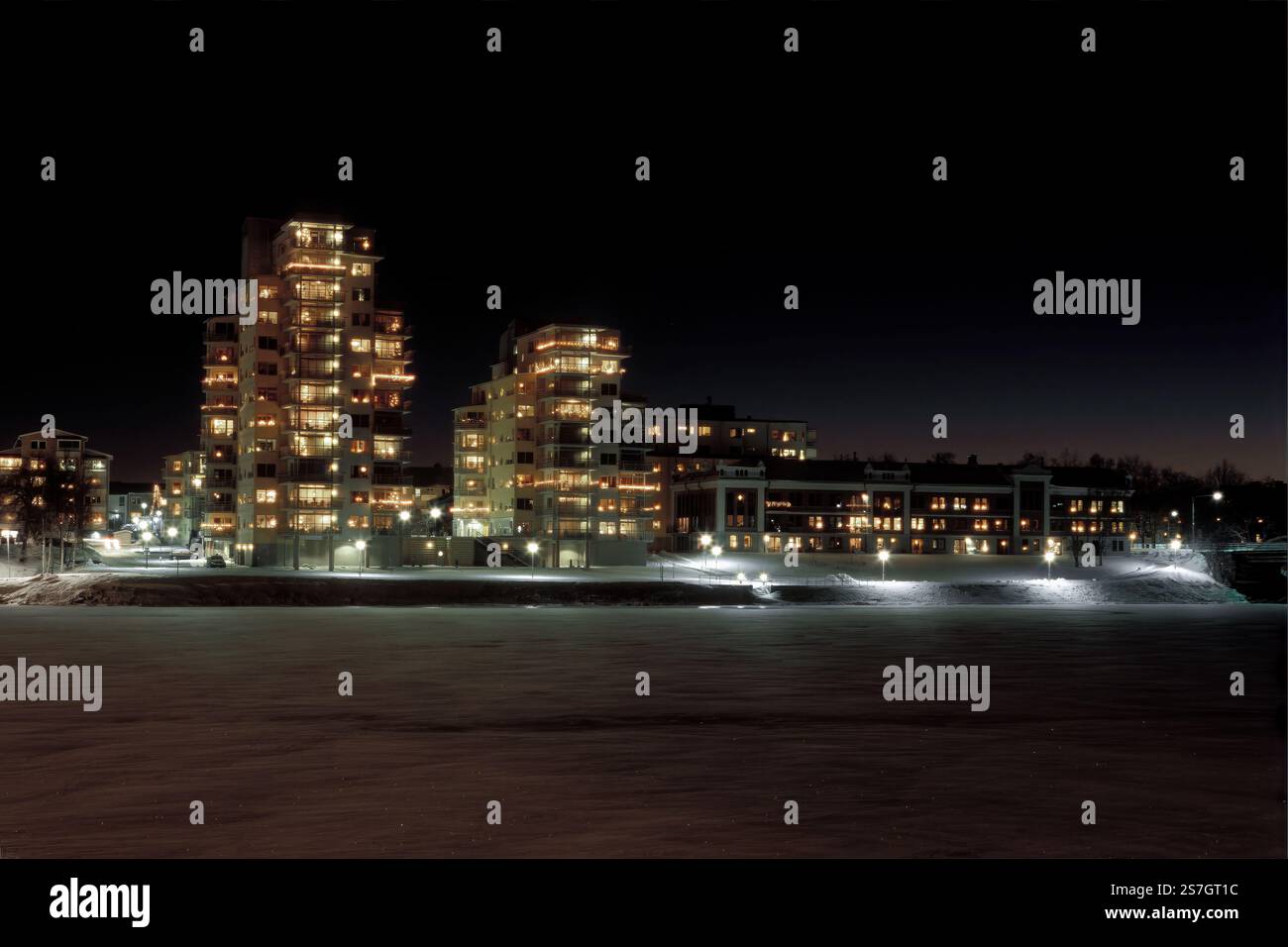 Night view of buildings, apartments, homes by a river. Lights in ...
