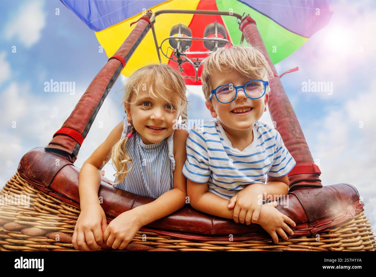 Two children lean over the edge of a wicker hot air balloon basket ...