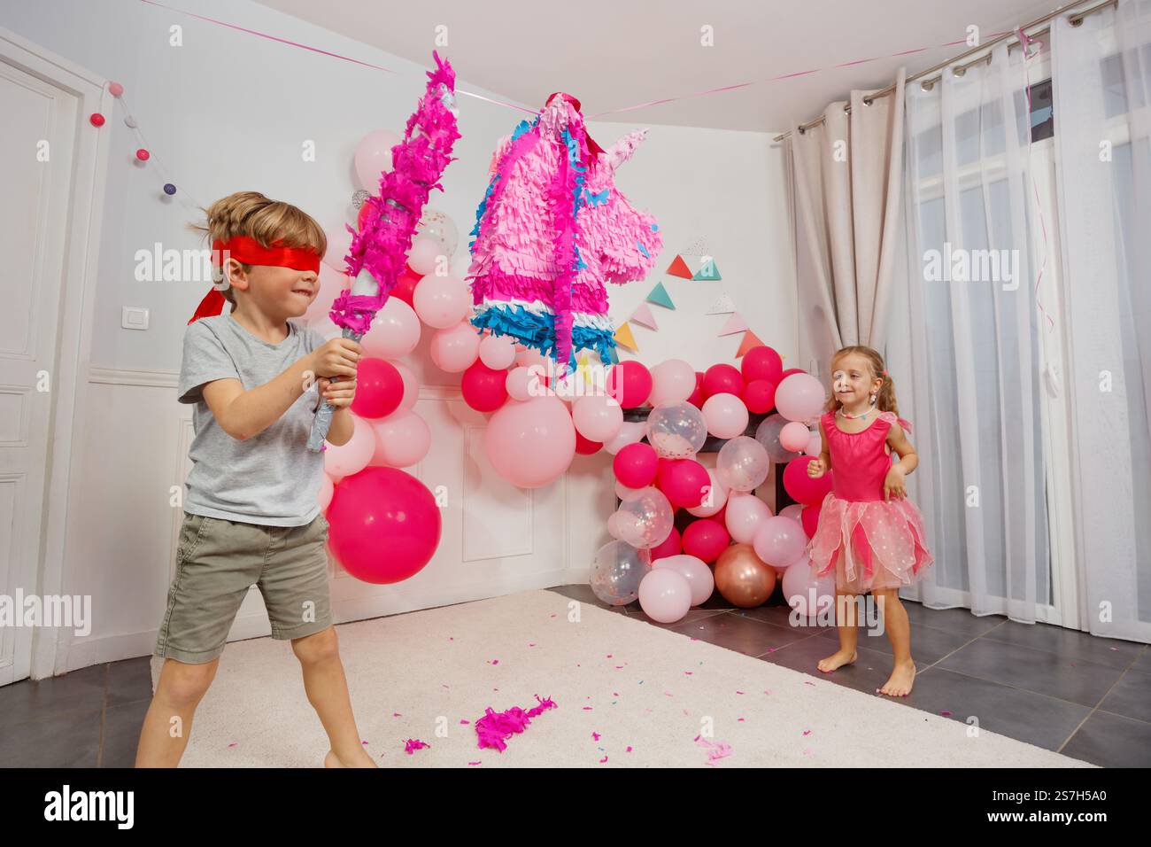 Kids have fun breaking a pink unicorn pinata at indoor party Stock ...