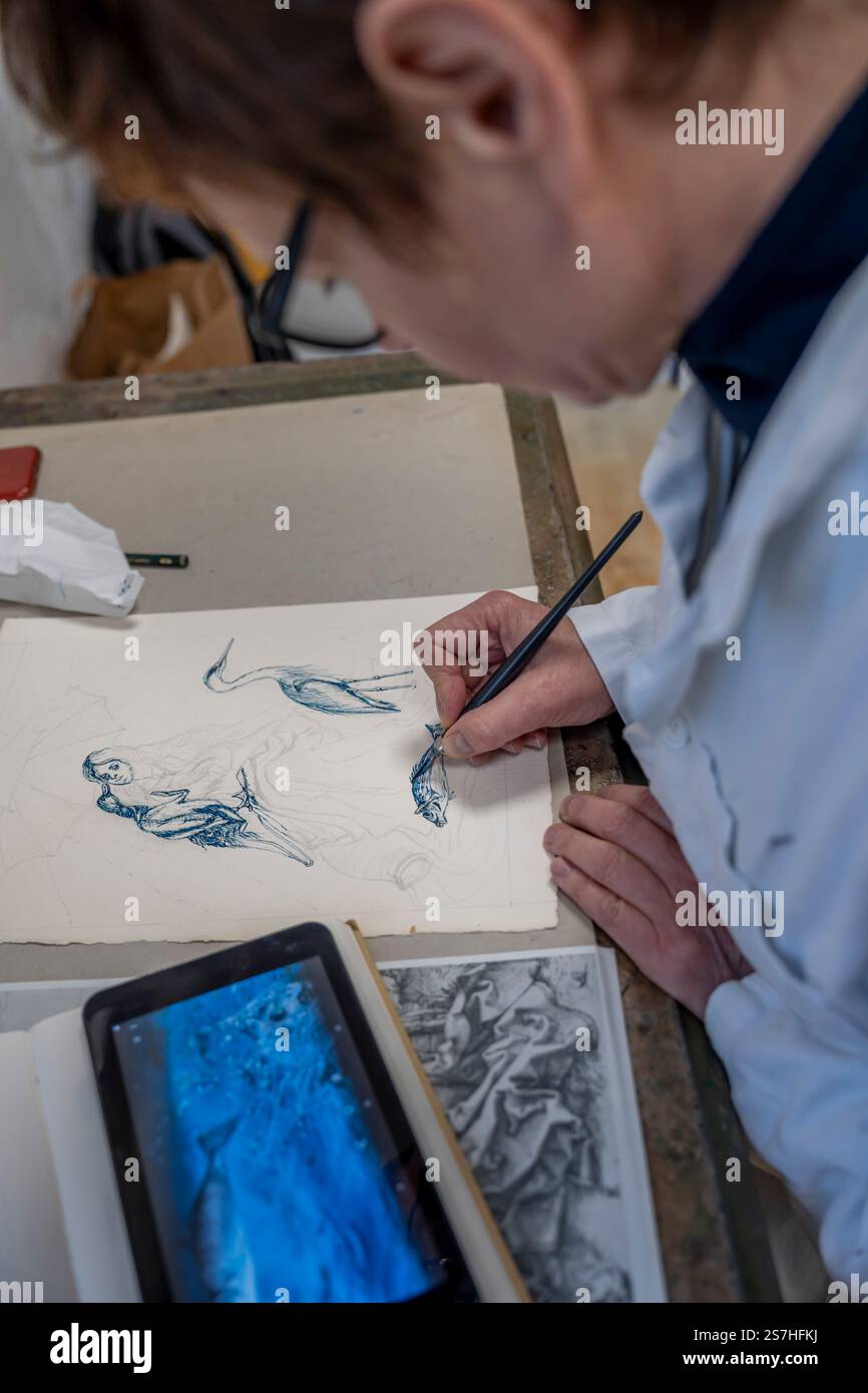 A mature woman with glasses draws a fish in ink with a quill pen during ...
