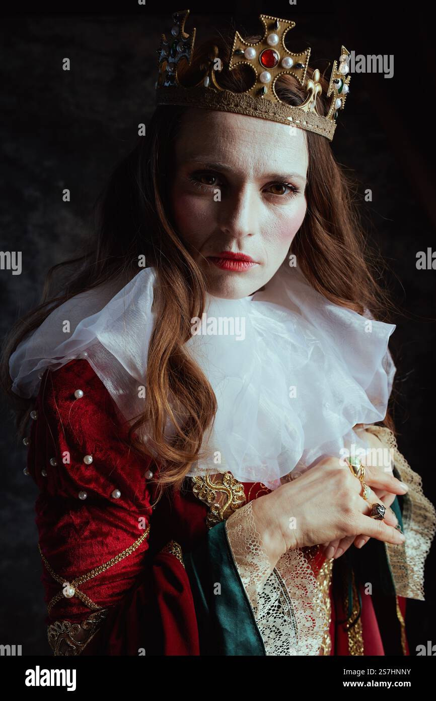 scary medieval queen in red dress with white collar and crown on dark ...
