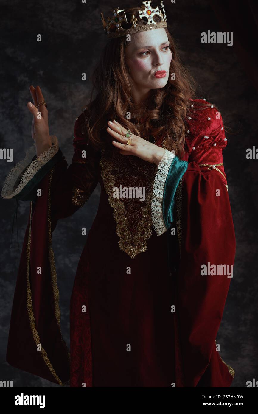 medieval queen in red dress with white makeup and crown on dark gray ...