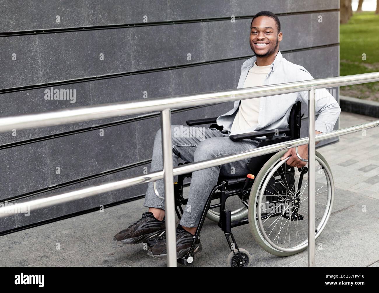 Happy impaired black man in wheelchair entering building on ramp ...