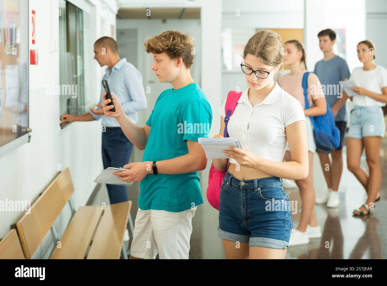 Teenage students checking exam schedule on bulletin board in college ...