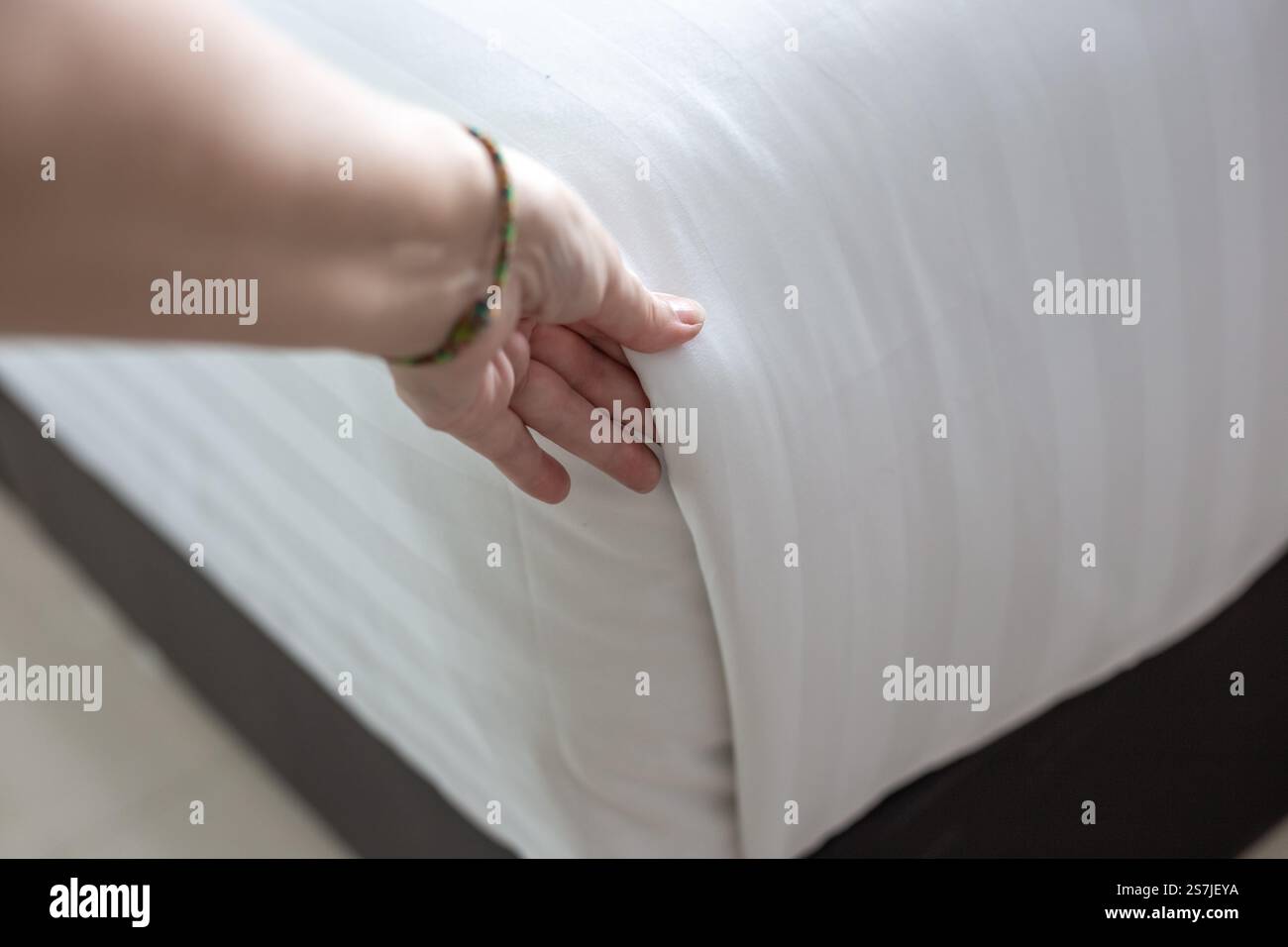 A maid makes a bed in a hotel room, tucking and straightening the ...