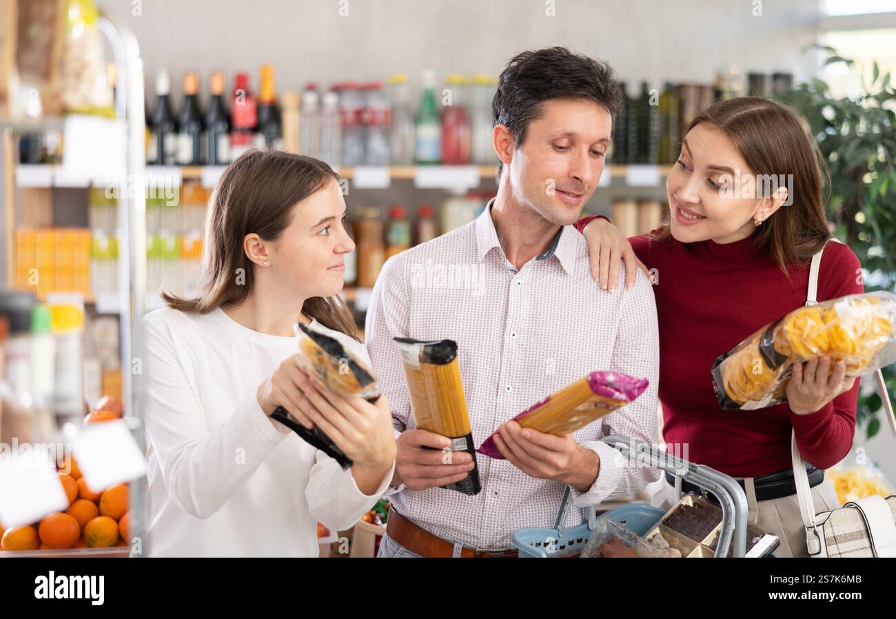 Dad, mom and daughter look at and choose pasta in selling area of shop ...