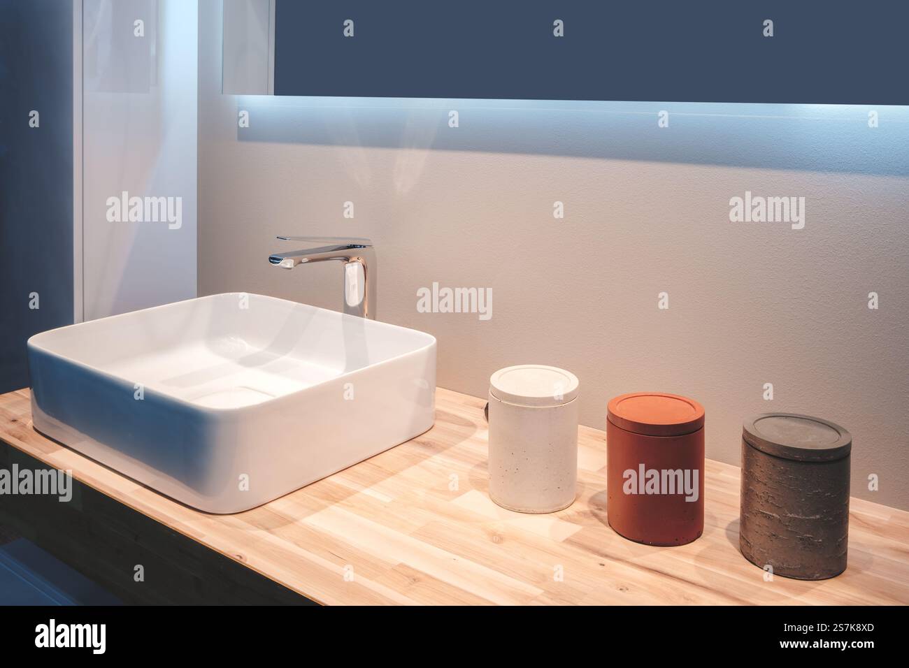 A white sink sits on a wooden countertop with three containers next to ...