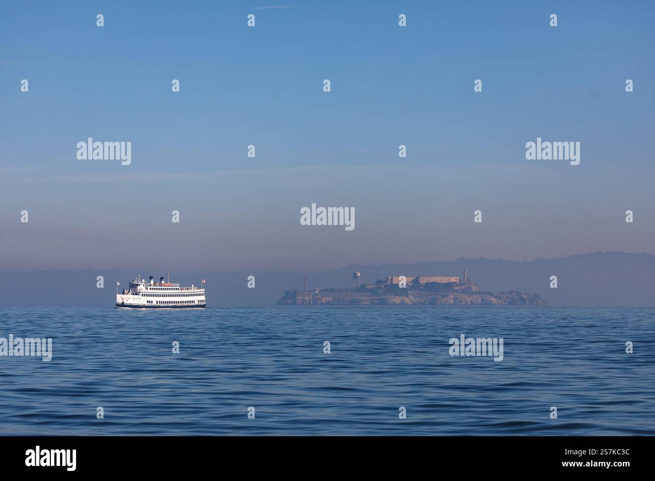 Alcatraz Island and ferry boat seen through fog in cool blue winter ...