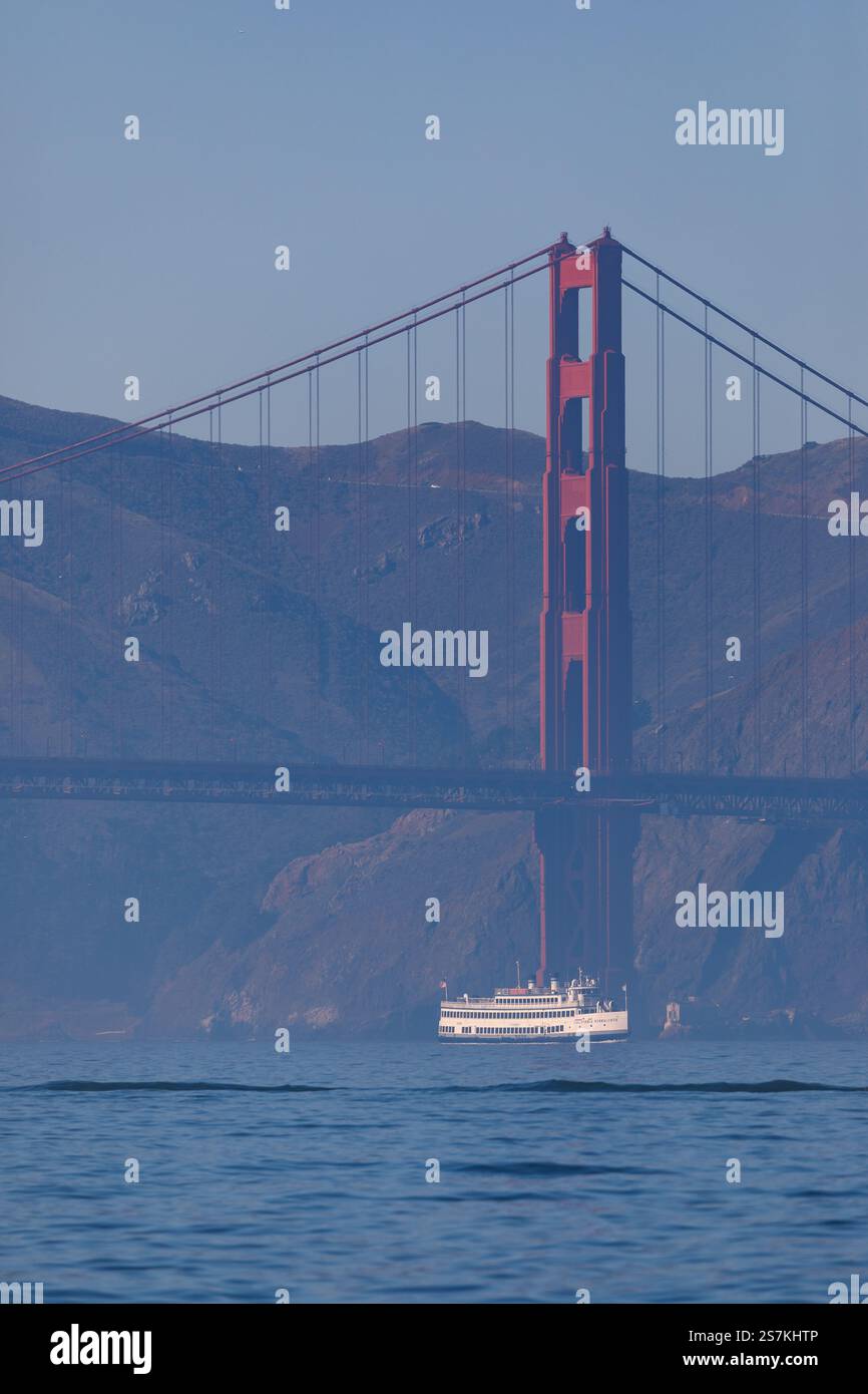 Ferry boat passes beneath the long and colorful span of Golden Gate ...