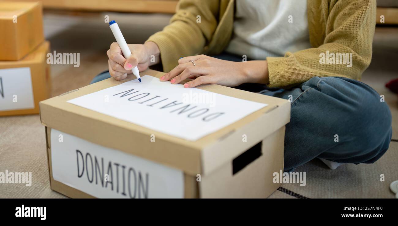 Woman labeling a donation box with marker while organizing clothes in a ...