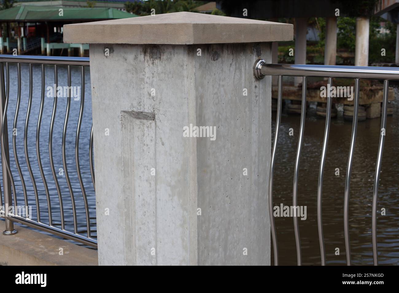 concrete pillar supporting shiny chrome guard rails along a river bank ...