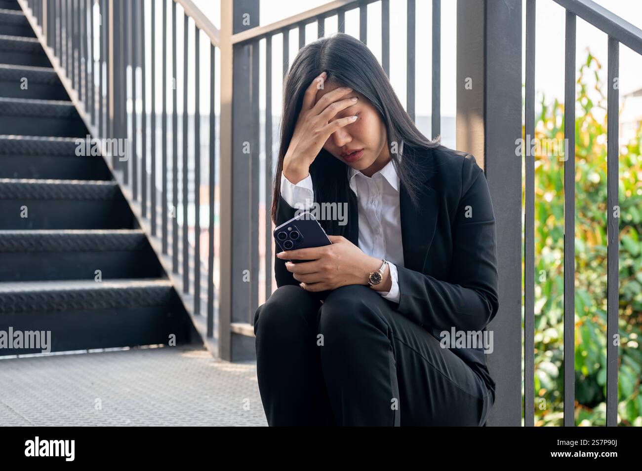 A stressed, overwhelmed Asian businesswoman sits on the stairs ...