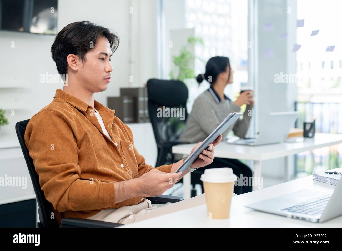 A smart, handsome Asian male office worker focuses on reading a ...