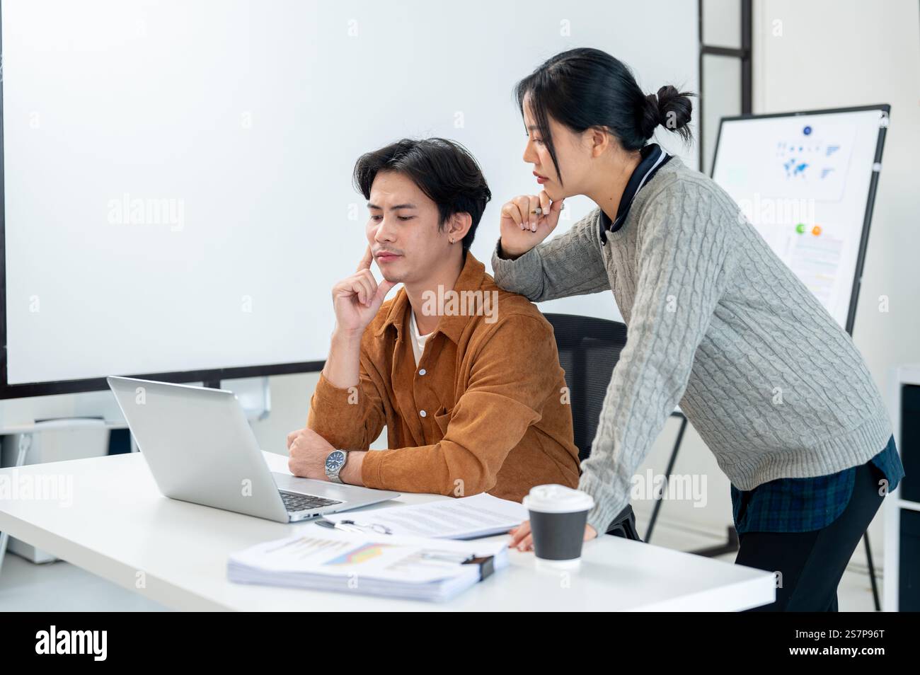 Two focused and serious Asian businesspeople look at a laptop screen ...