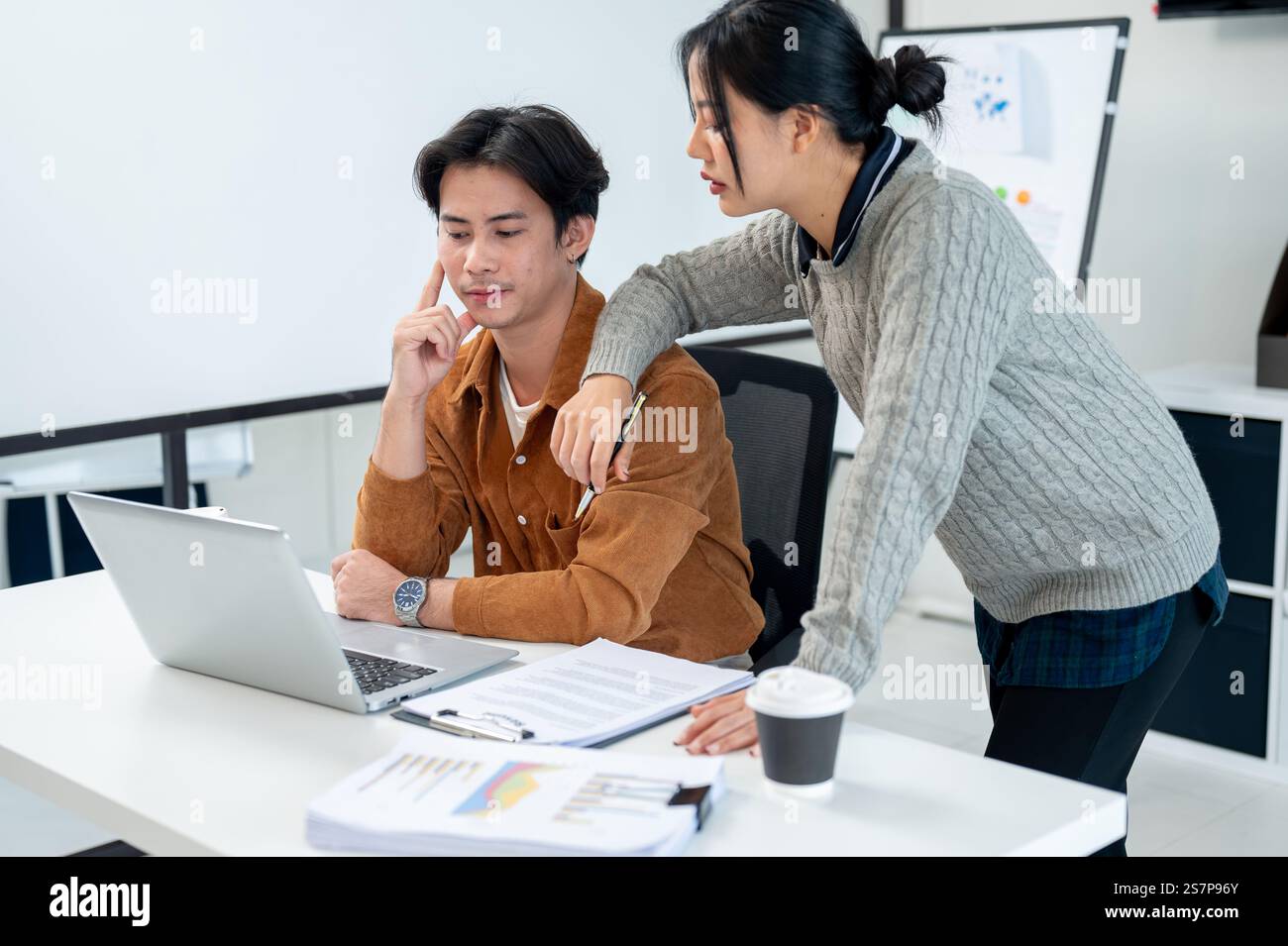 Two focused and serious Asian businesspeople look at a laptop screen ...
