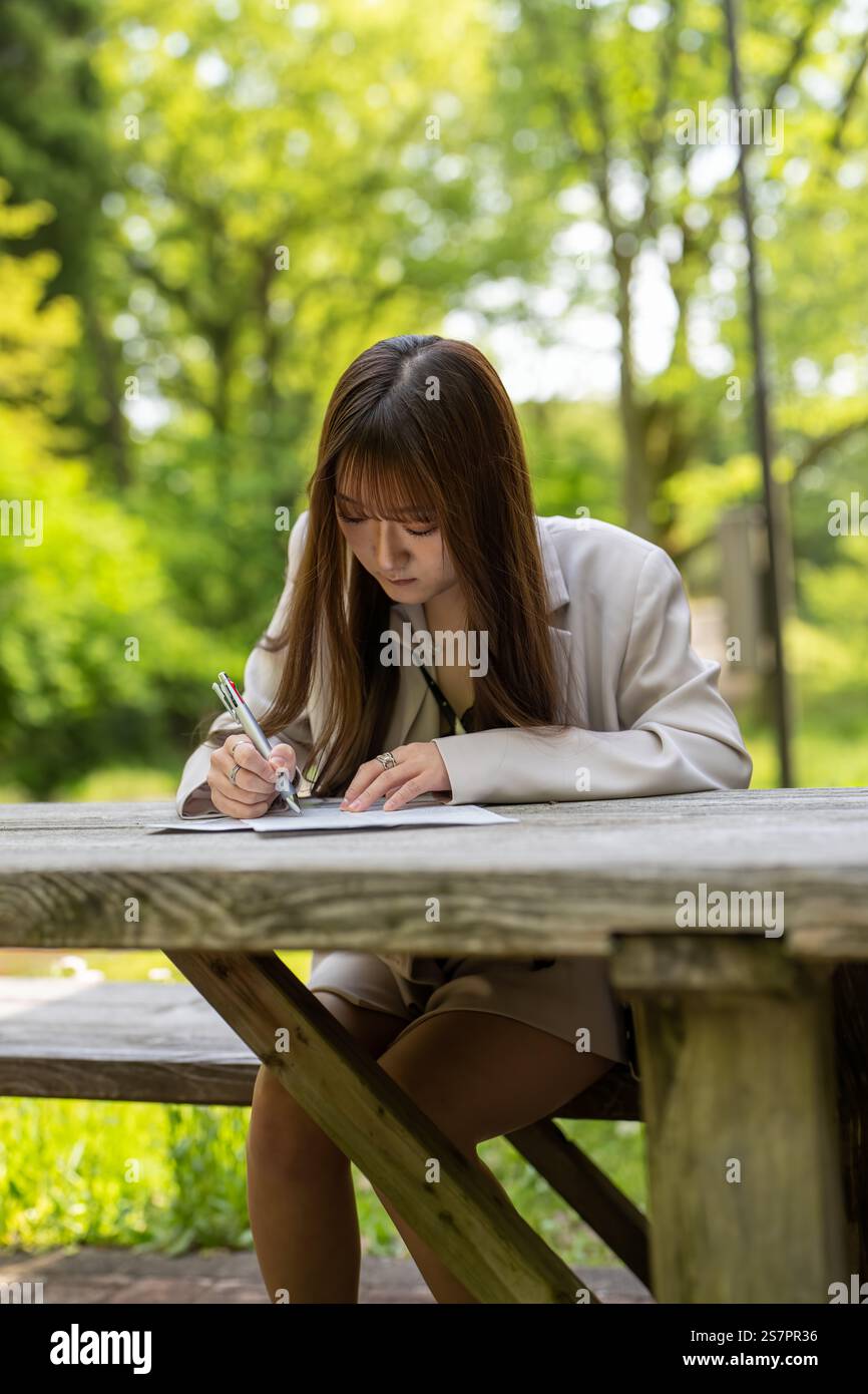 A Japanese woman in her 20s wearing white clothes sits at a desk in ...