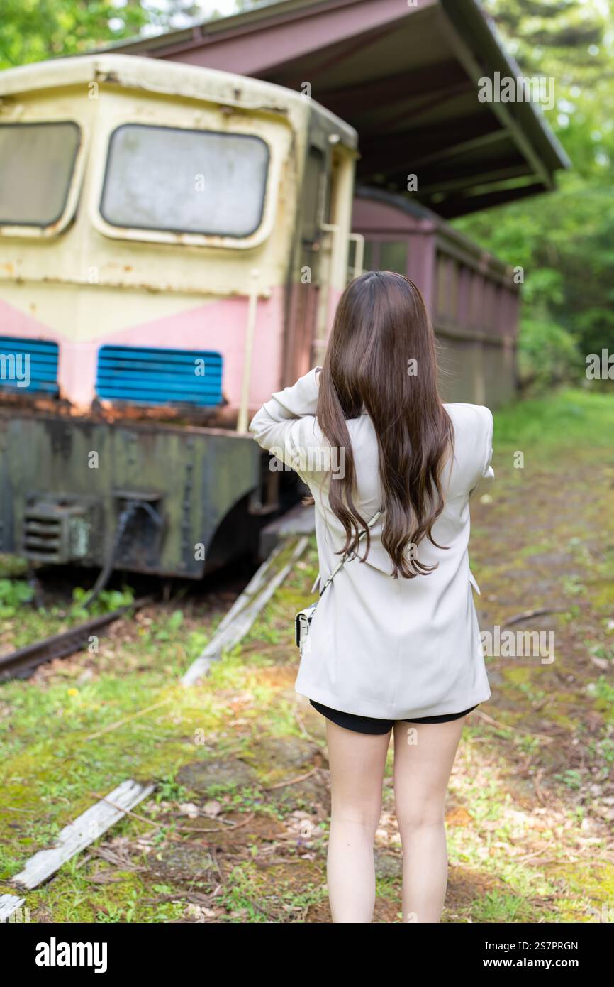 A Japanese woman in her 20s wearing white clothes spends her time on an unused train in a park ...