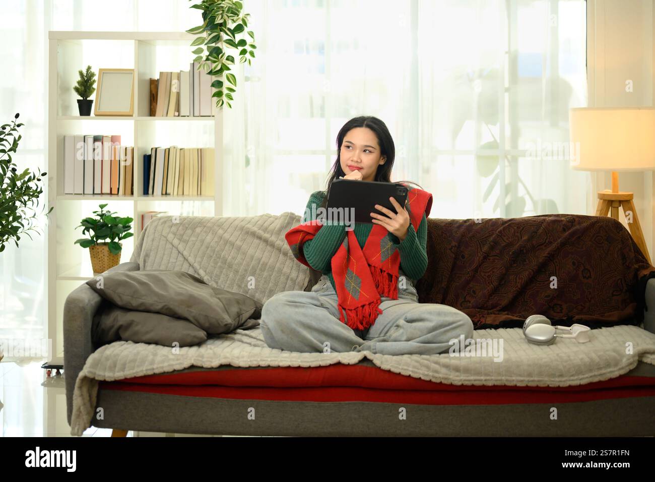 Pretty young woman sitting on a sofa holding digital tablet tablet ...