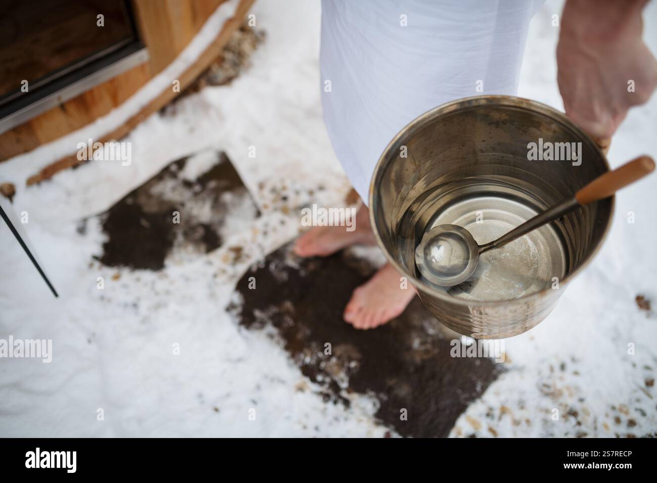 Older man entering small sauna, carrying bucket of water to create ...