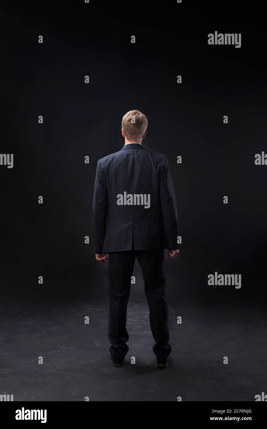 In a dark studio, a man stands confidently in a crisp black suit and ...