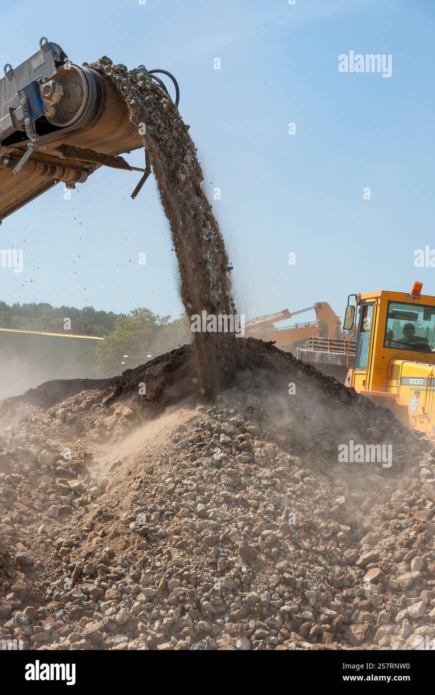 Crushed stones fall from a conveyor. In the background a Volvo wheel ...