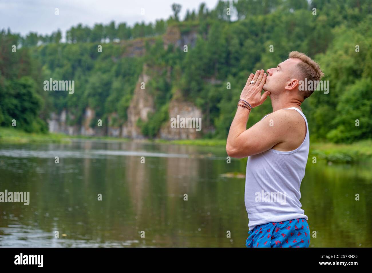 Mindful man meditates with hands in prayer position by a tranquil river ...
