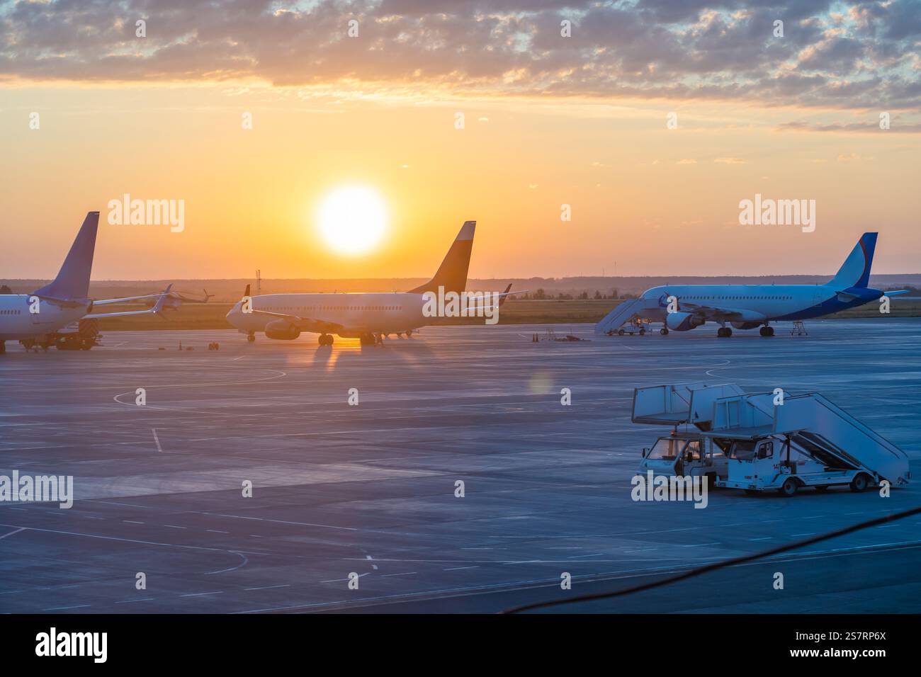 Passenger jets resting on airport tarmac, golden sunrise illuminating ...