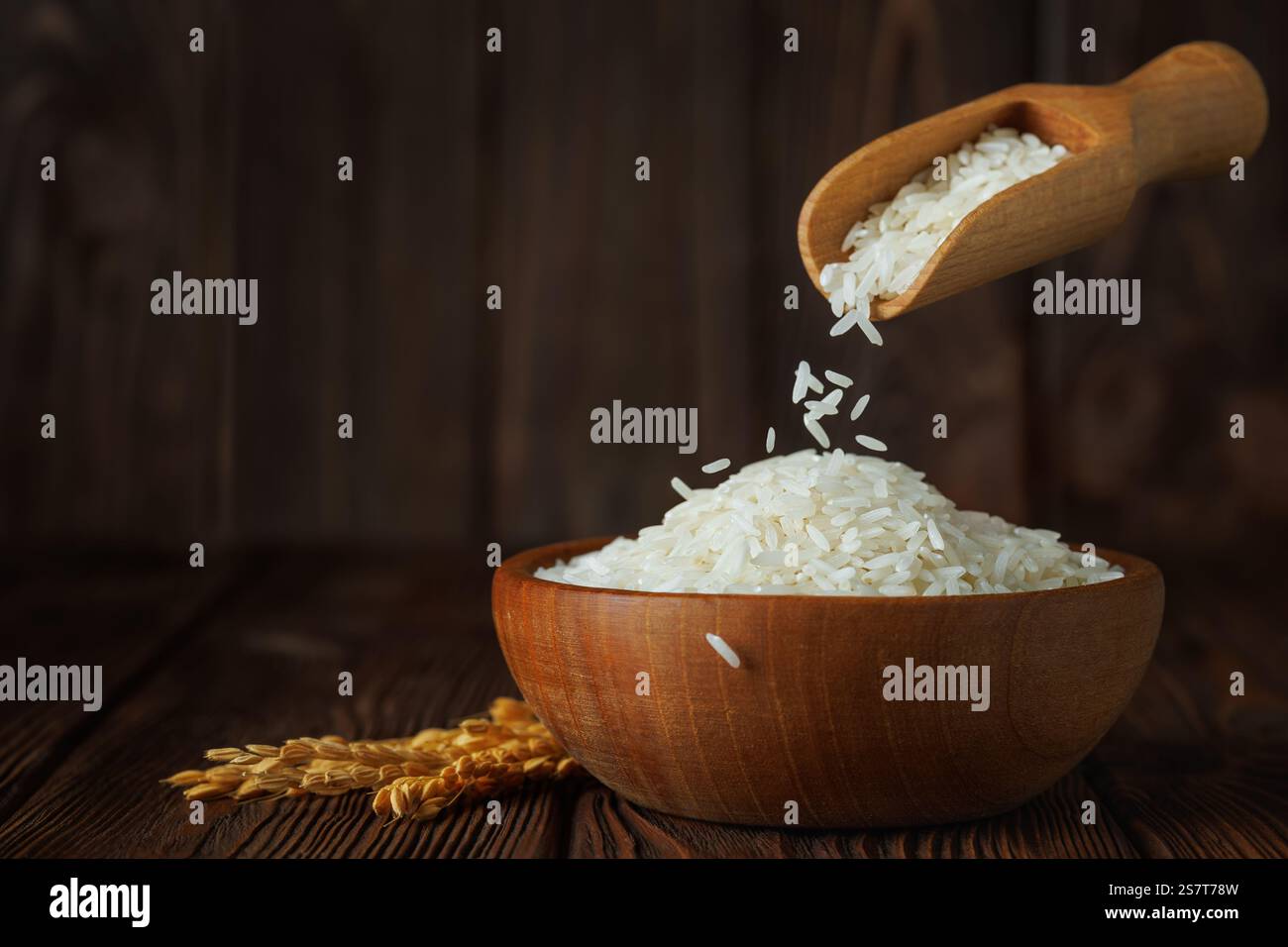 rice falling from scoop in bowl with ears near on wooden background ...