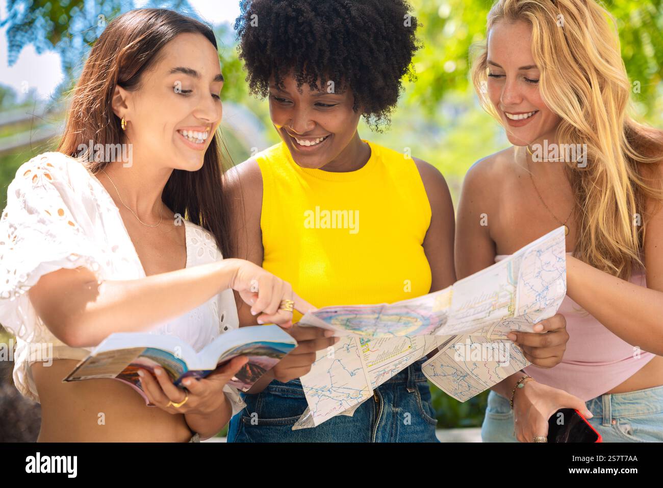 Three young women exploring a city with maps and a travel guide ...