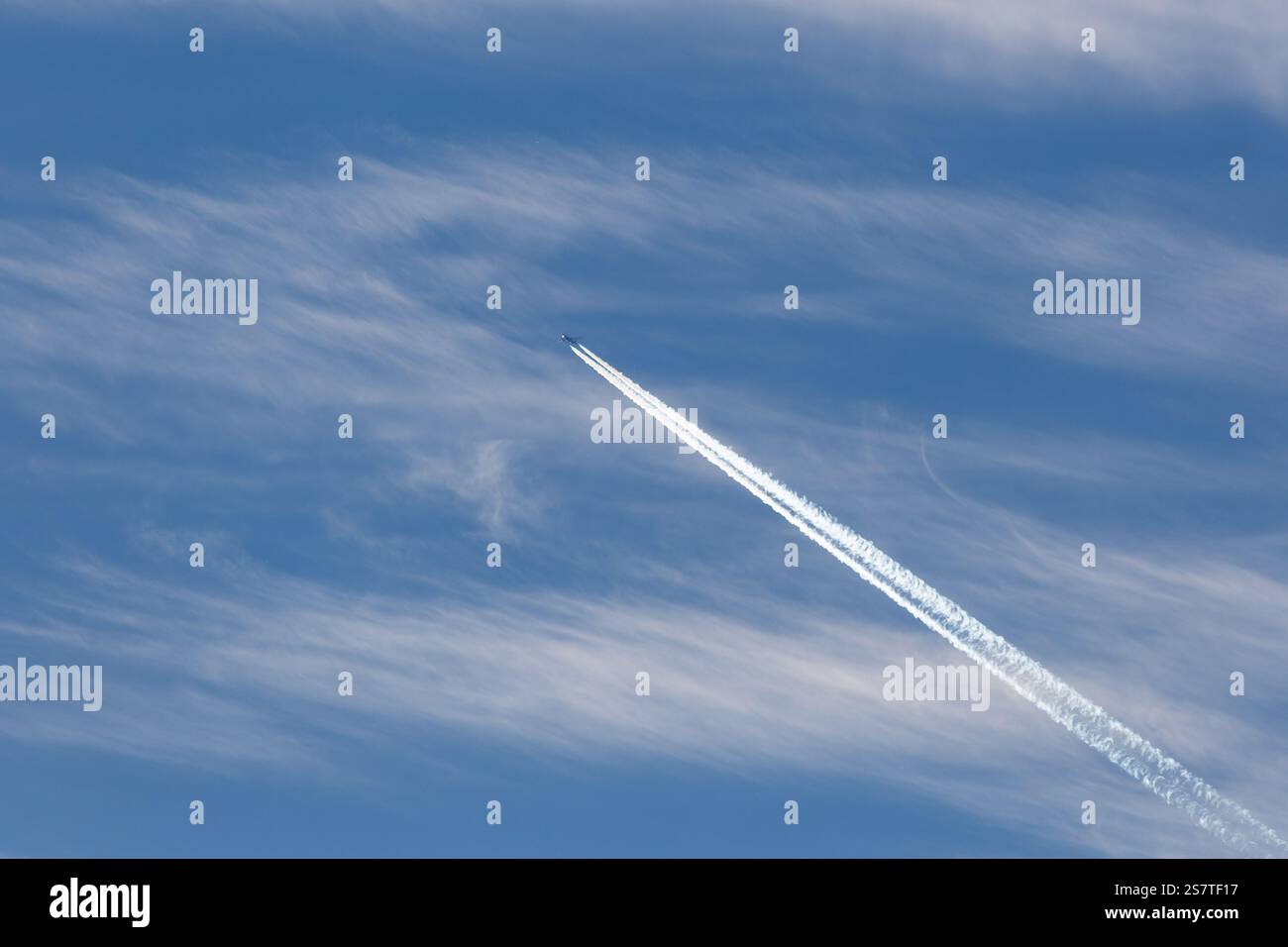 A jet plane leaves a contrail in a blue sky with cirrus clouds Stock ...
