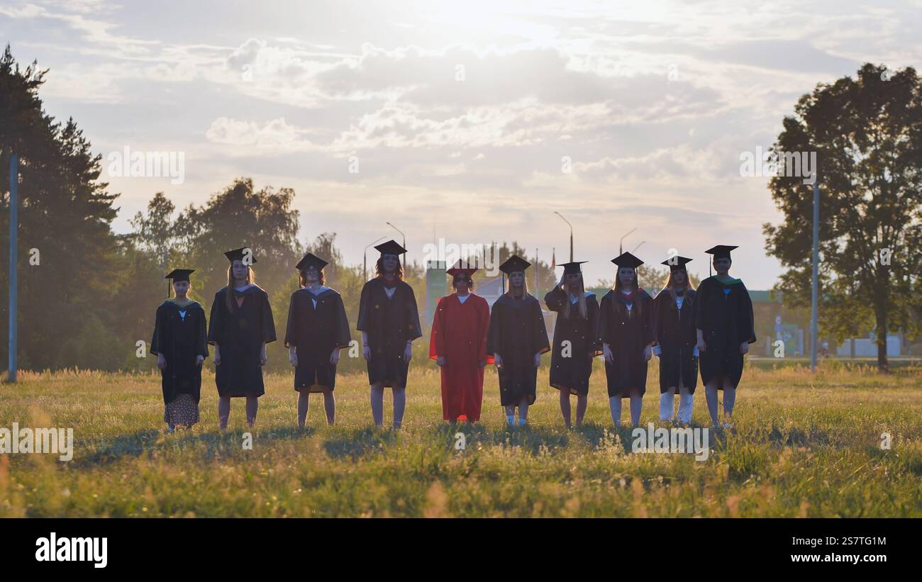 Graduates wearing their caps and gowns are jumping for joy in a field ...
