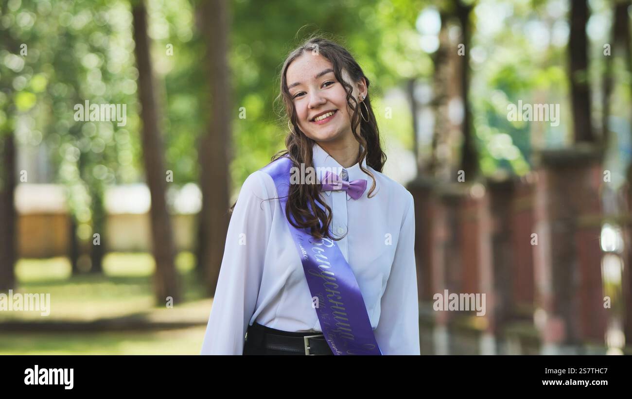 Happy graduate student in a park wearing a purple graduation sash and ...