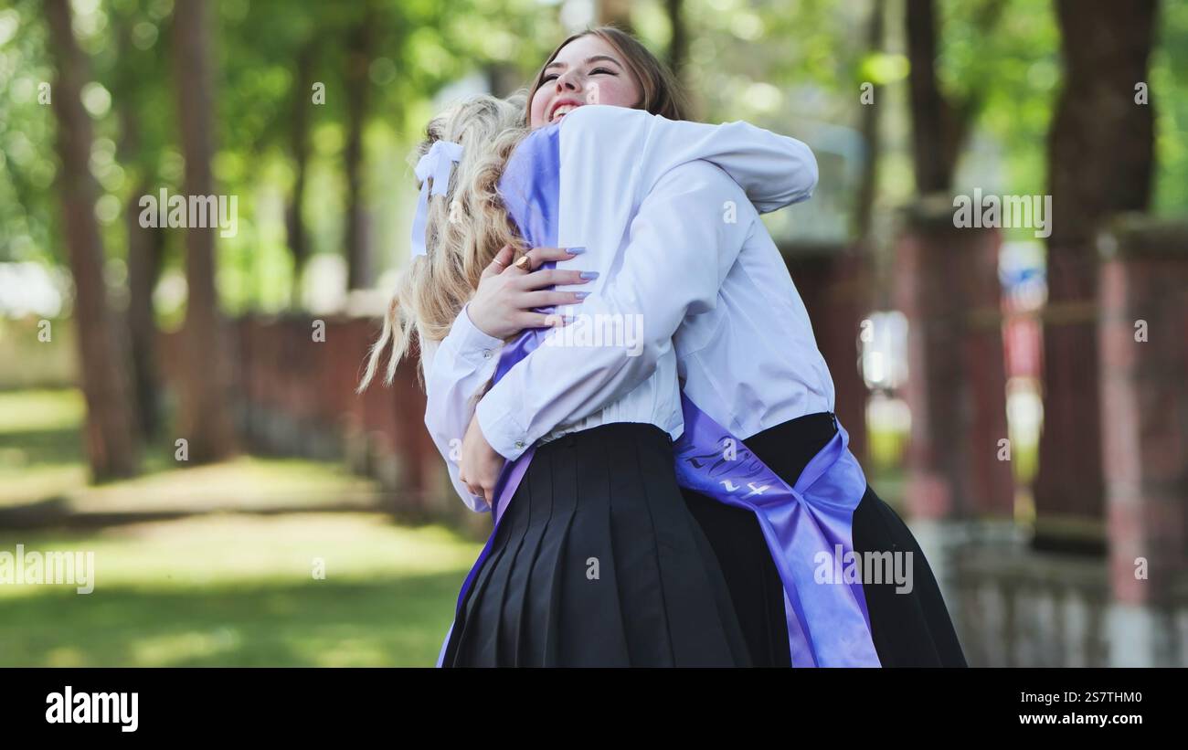 Two joyful female graduates hugging with sashes on their last day of ...