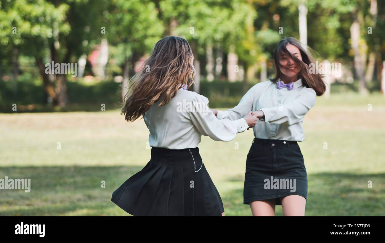 Two joyful schoolgirls holding hands and twirling in a park, embracing ...