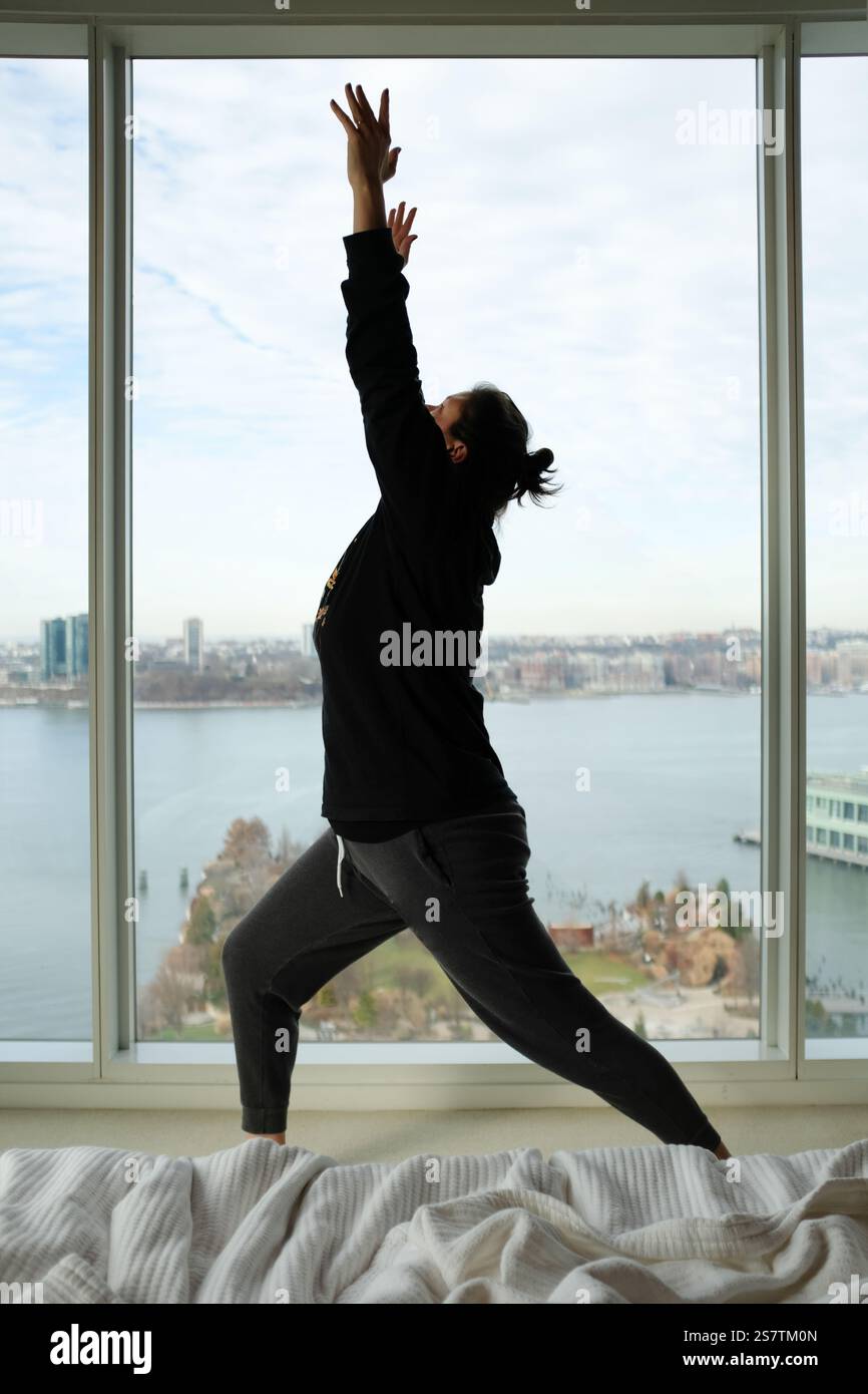 Woman in casual comfy clothes does yoga pose in front of hotel window ...