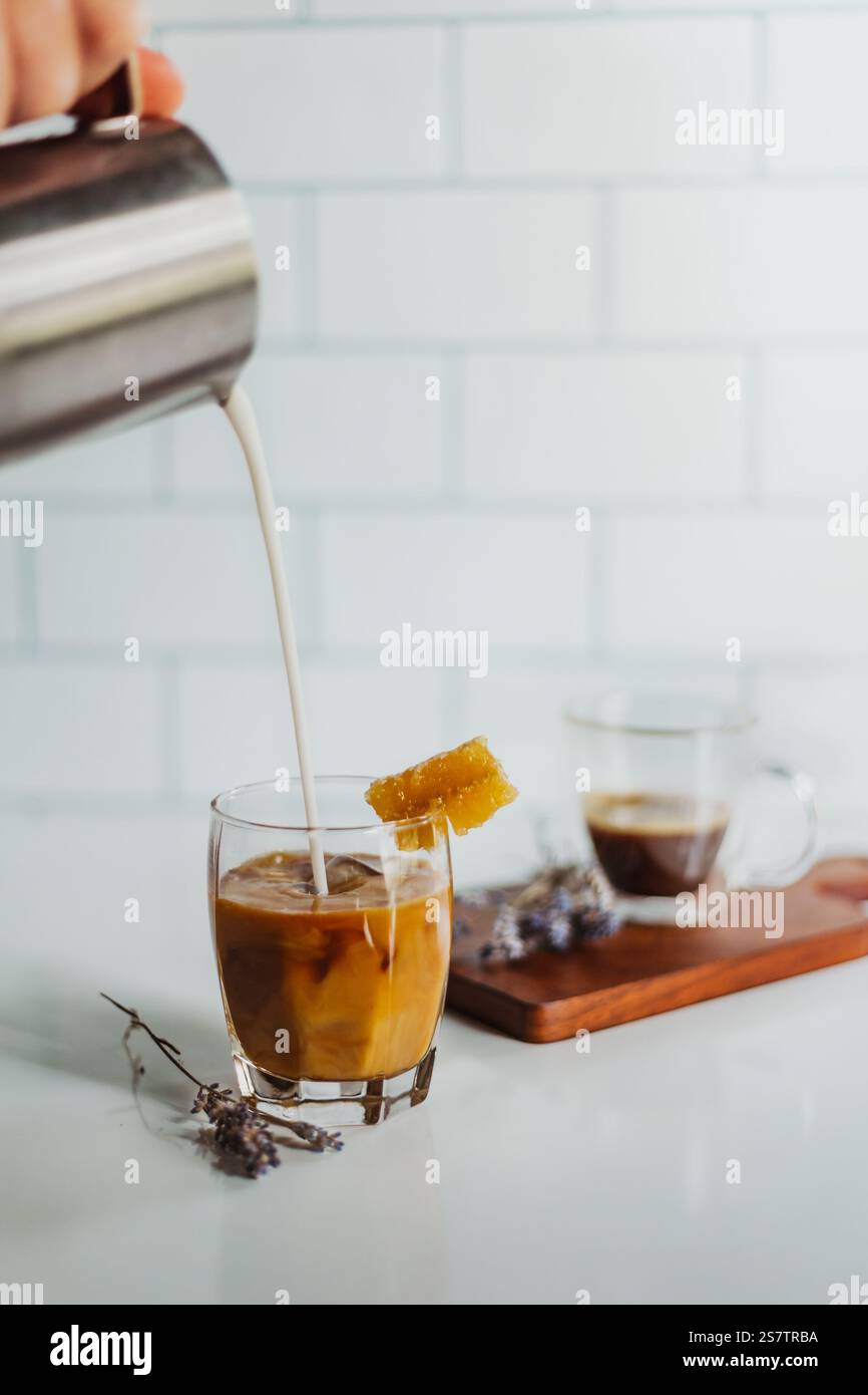 Milk being poured into coffee with honey rim in white clean kitchen ...