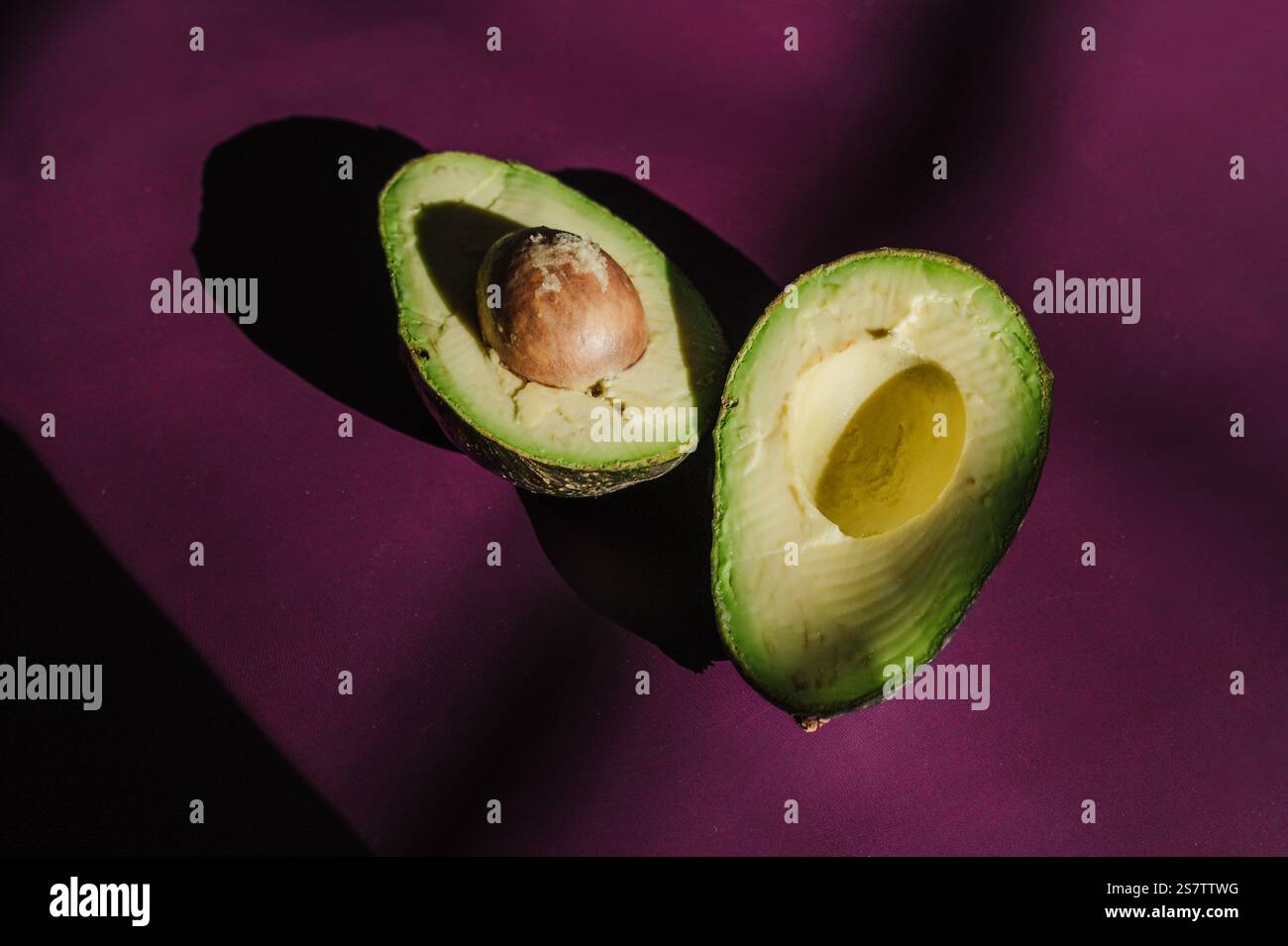 Avocado cut in half in dramatic light with purple background Stock ...