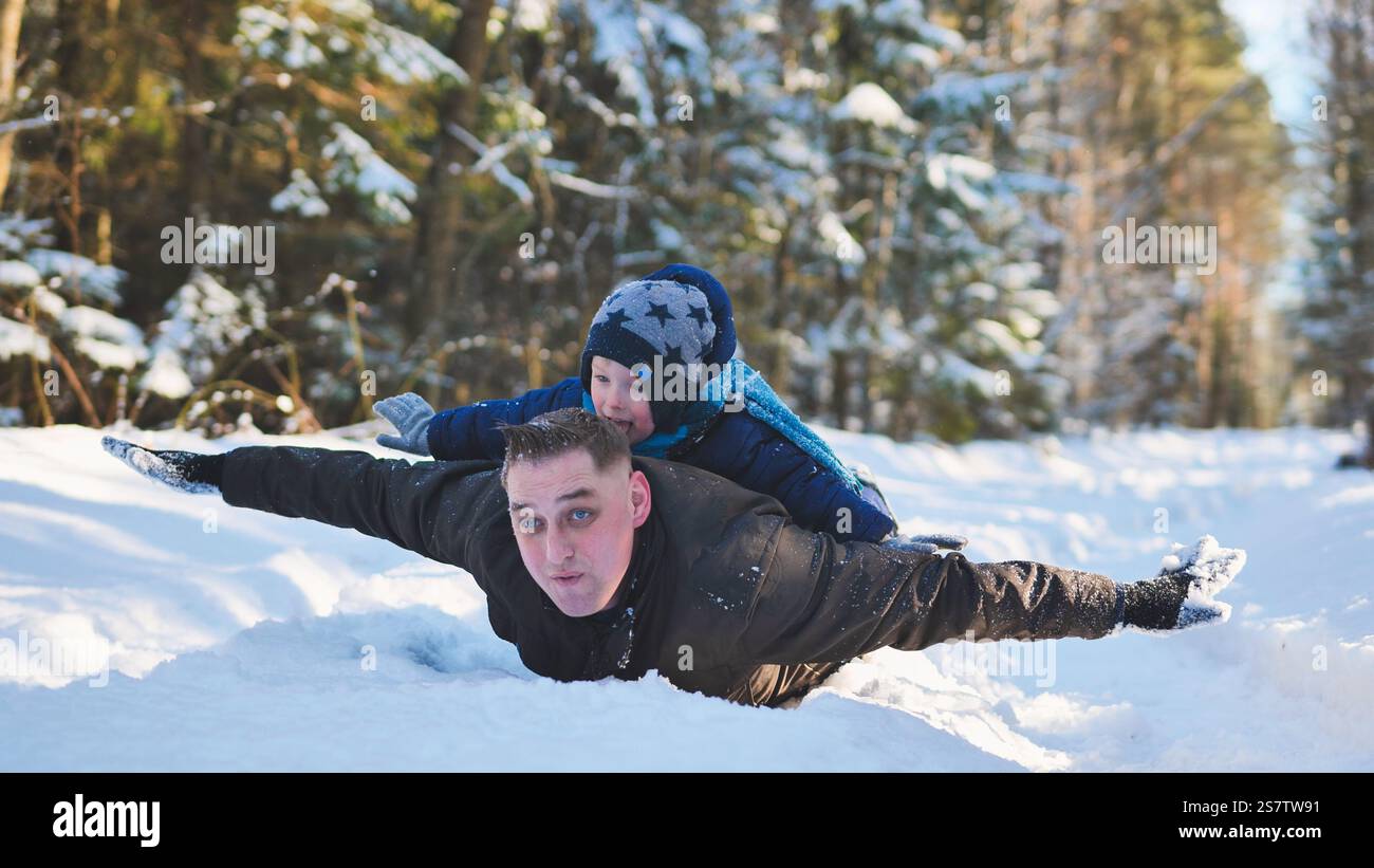Playful father carrying son piggyback, laughing while lying in snowy ...