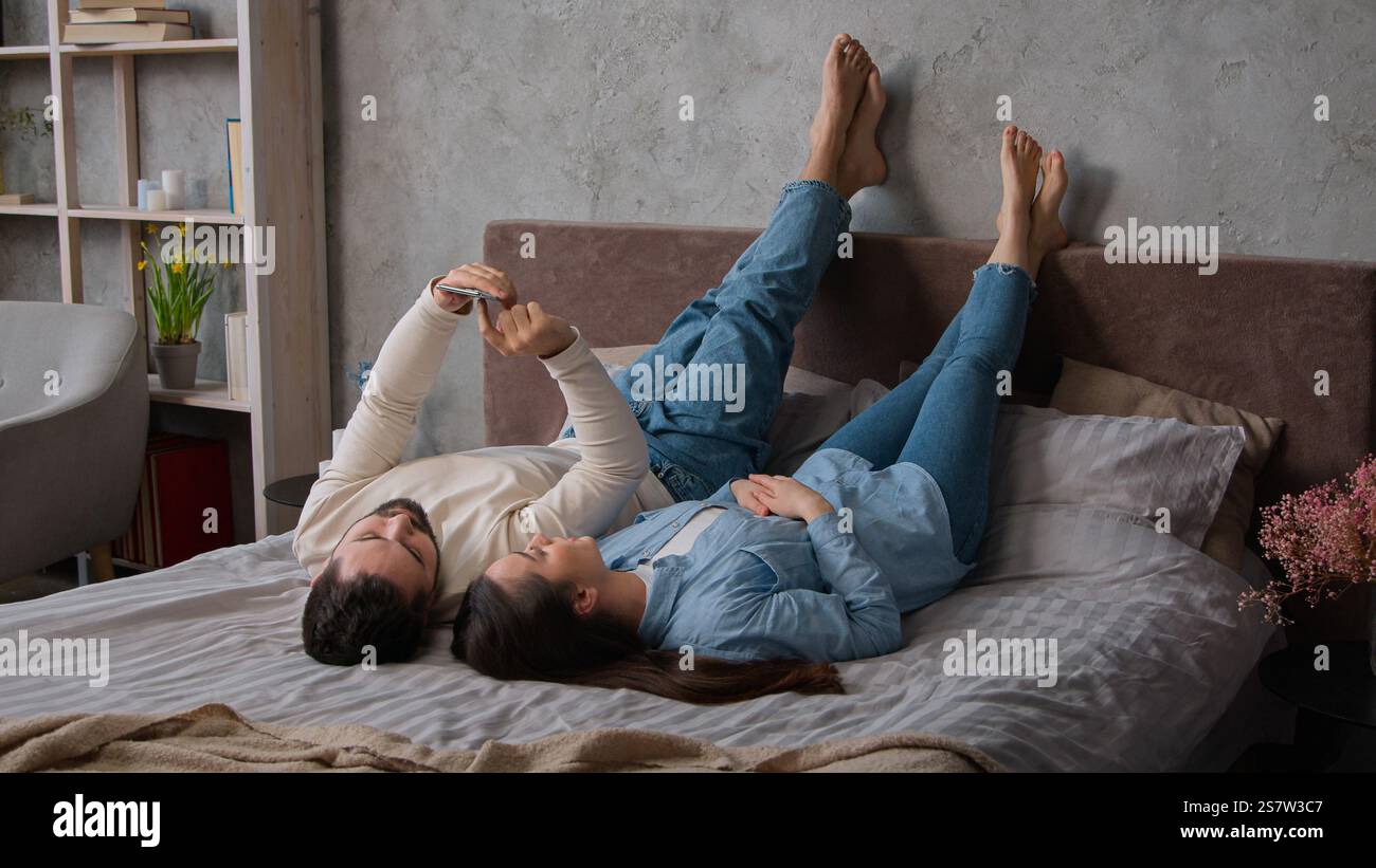 Carefree Caucasian couple in love lying down kick up feet on bed family ...