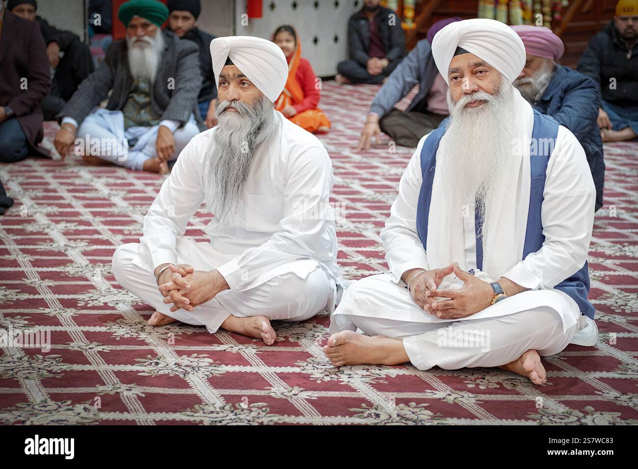 2 Sikh priests dressed in white sit and listed to a teenage group ...
