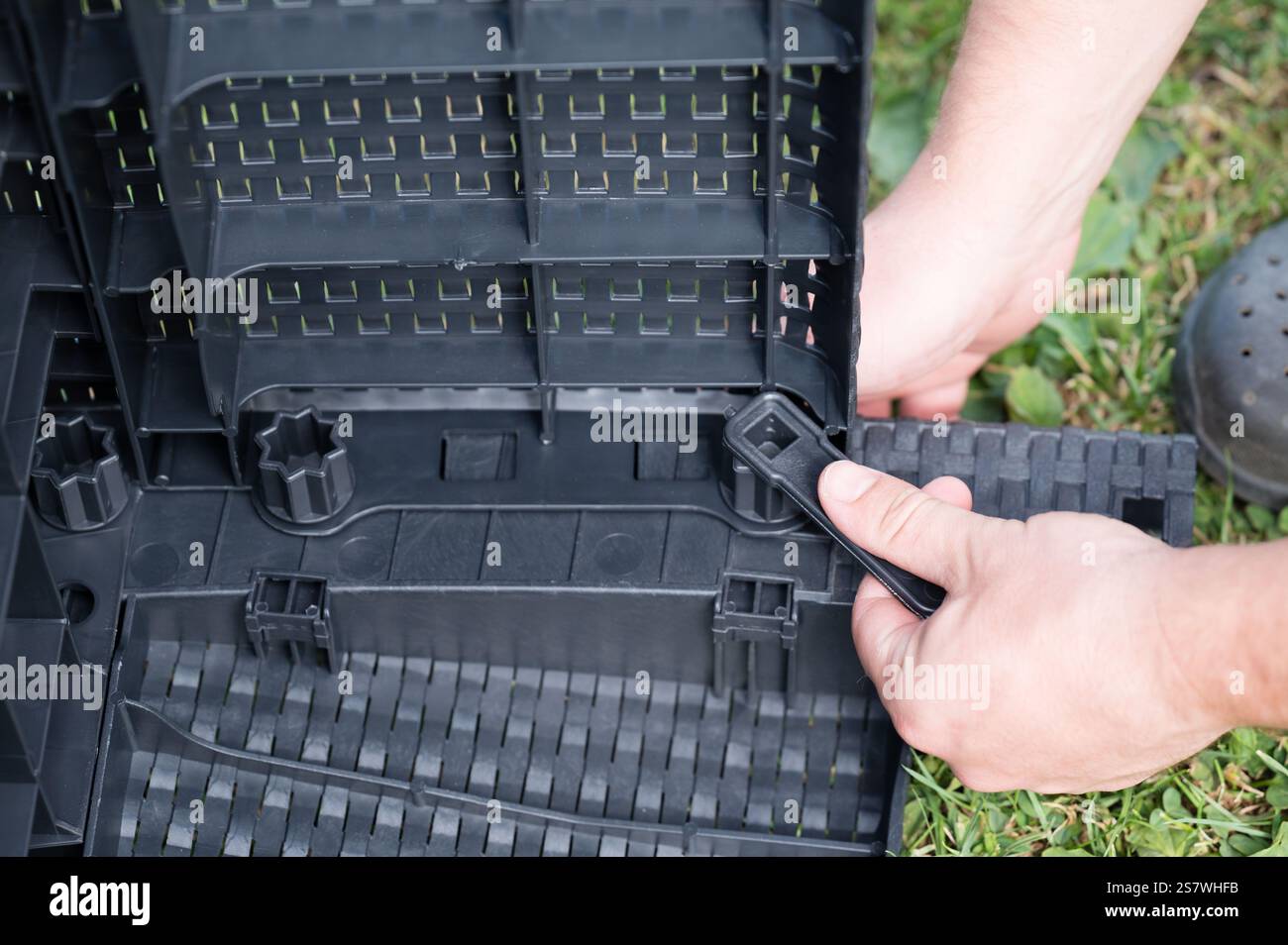 Close-up of hands assembling sections of a black plastic raised garden ...