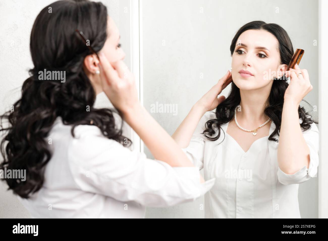 A woman with dark, wavy hair uses a hairbrush to style her locks while ...