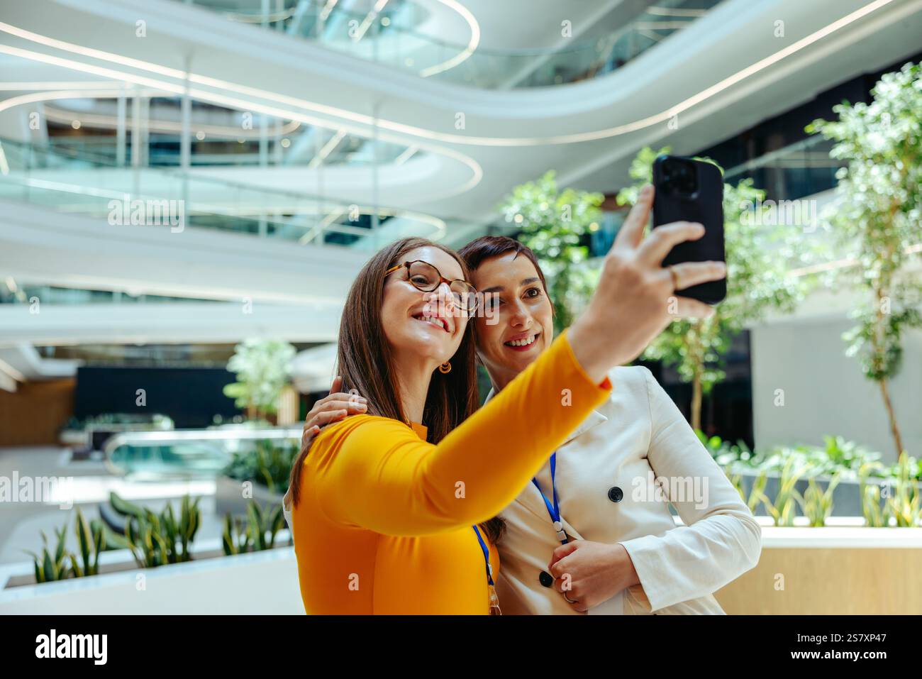 Two female colleagues pose for a selfie in a modern office setting on ...