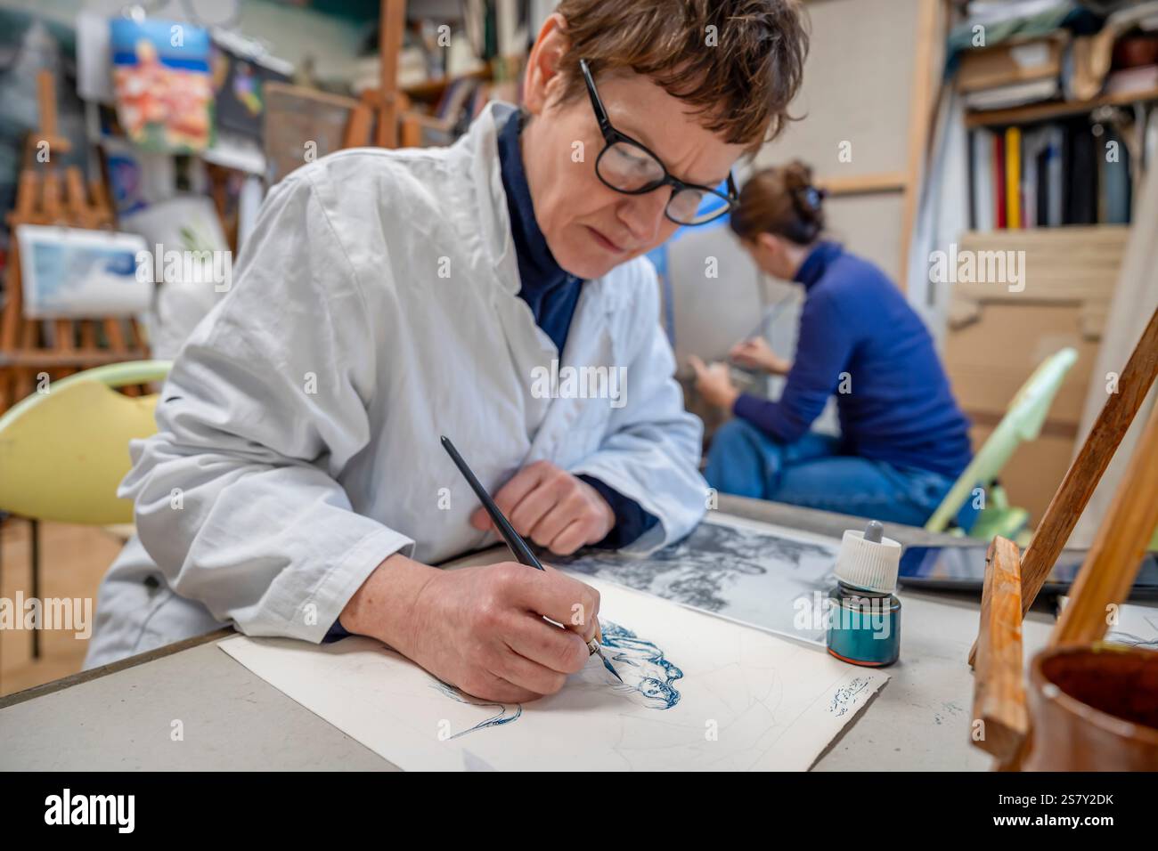 A mature woman with glasses draws a woman in blue ink with a quill pen ...