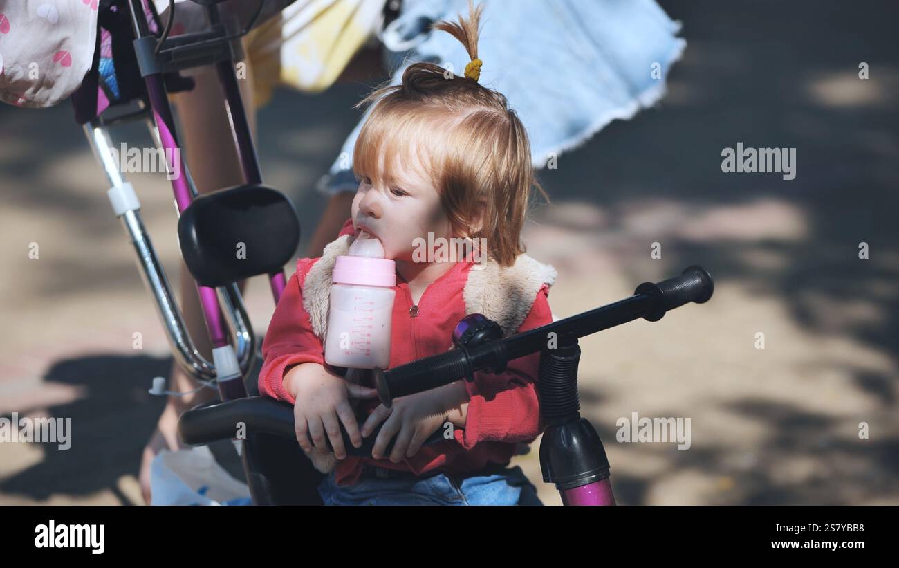 Smiling toddler sipping bottle while riding colorful tricycle on sunny ...