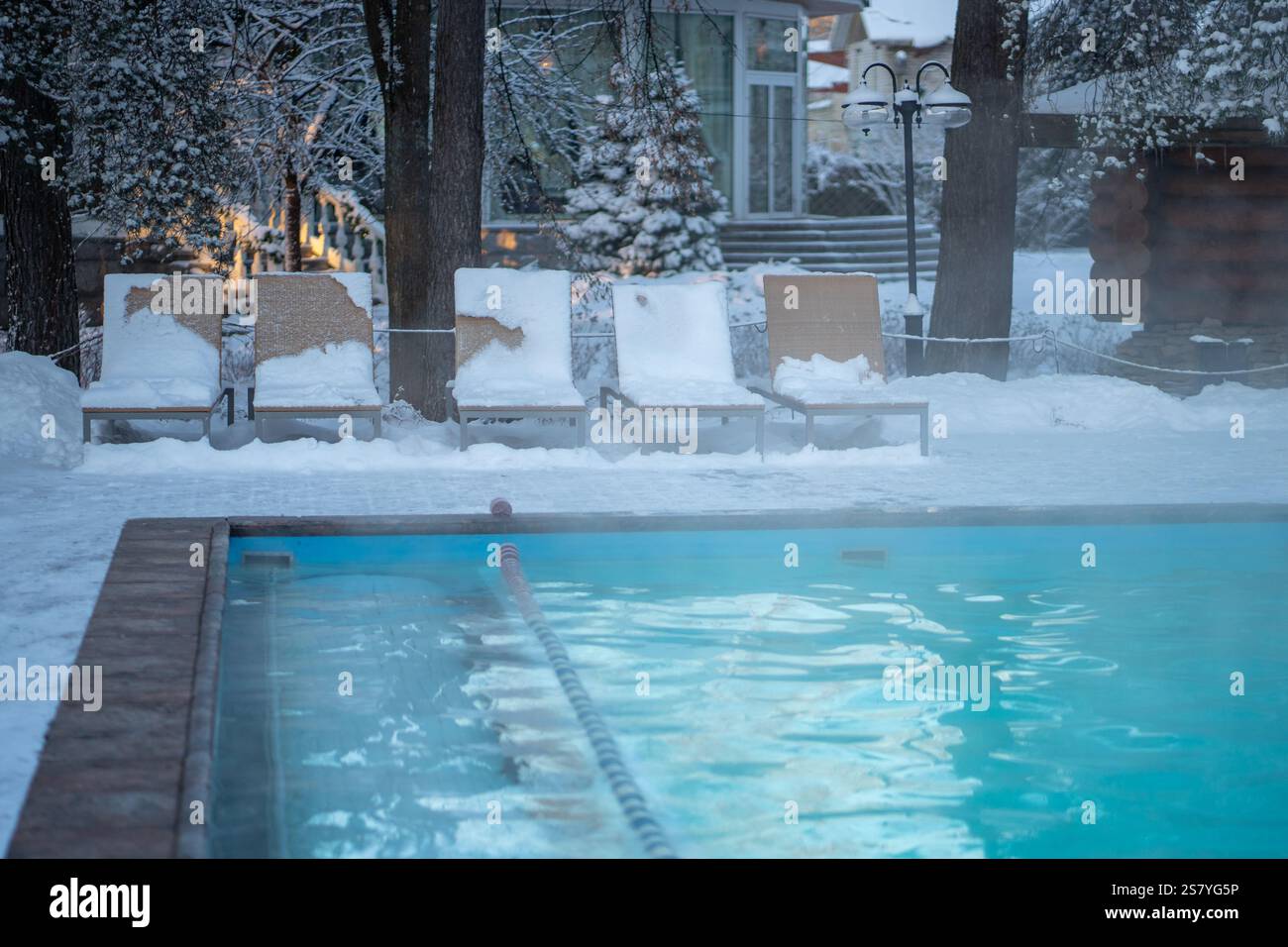 Open-air swimming pool with warm water, loungers in cold weather ...