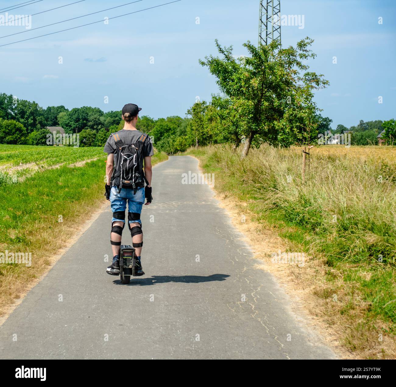 A man is riding a electric unicycle euc on a road. The sky is blue and ...