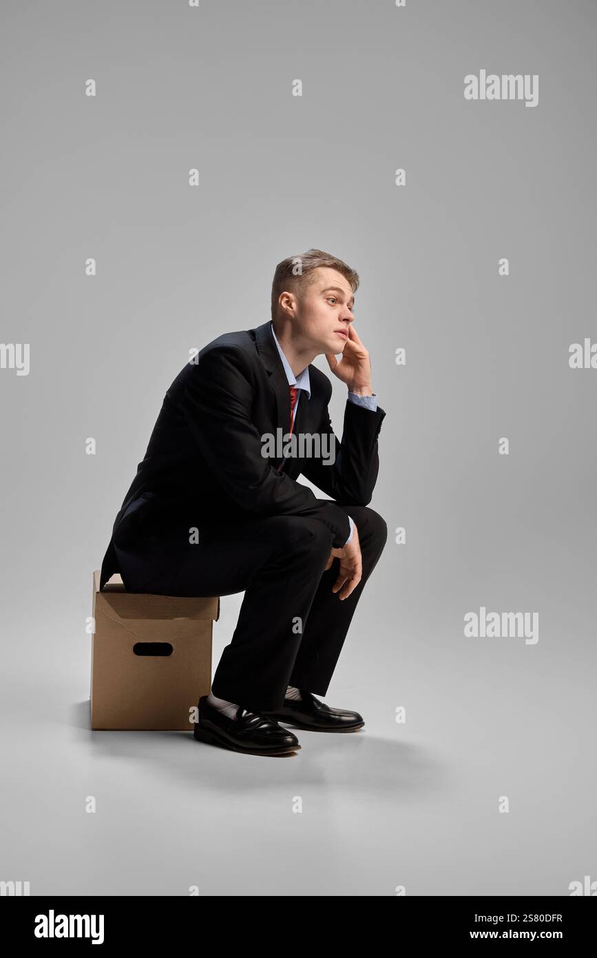 Man sitting on box, leaning forward, resting chin on hand, appearing ...